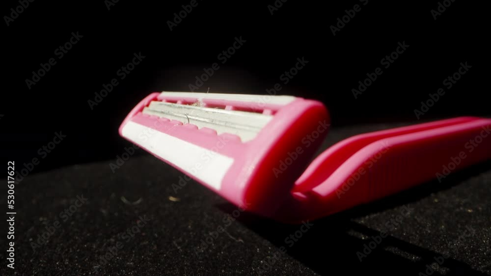 Pink disposable razor and stuck hair, on a black background. Dolly ...