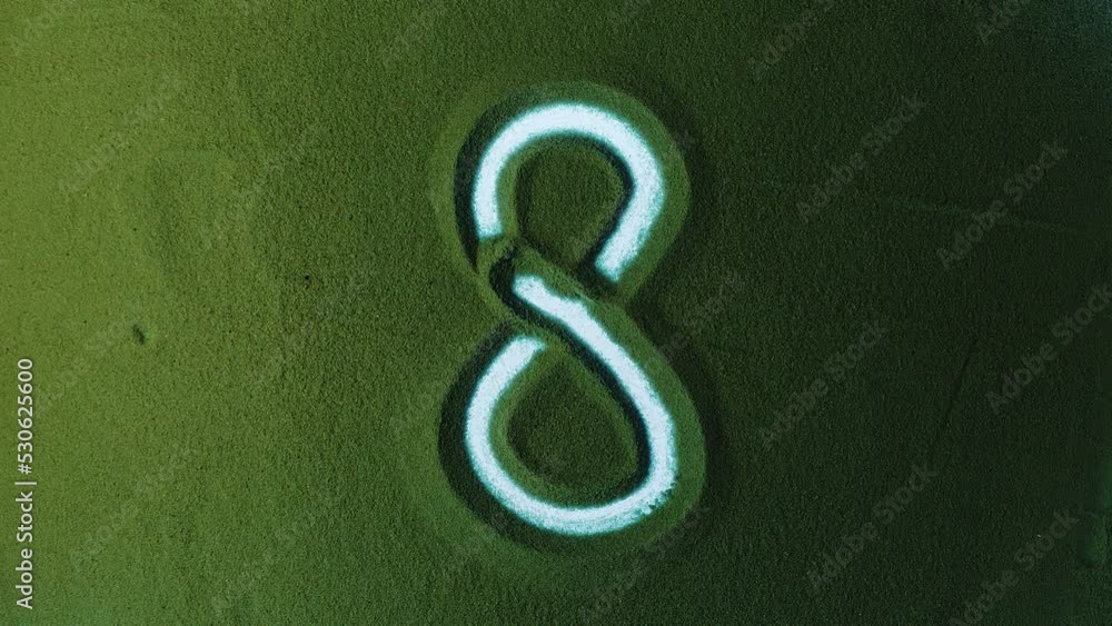 Hand drawing Number Eight 8 Symbol in the Green Sand. Male hand writes ...