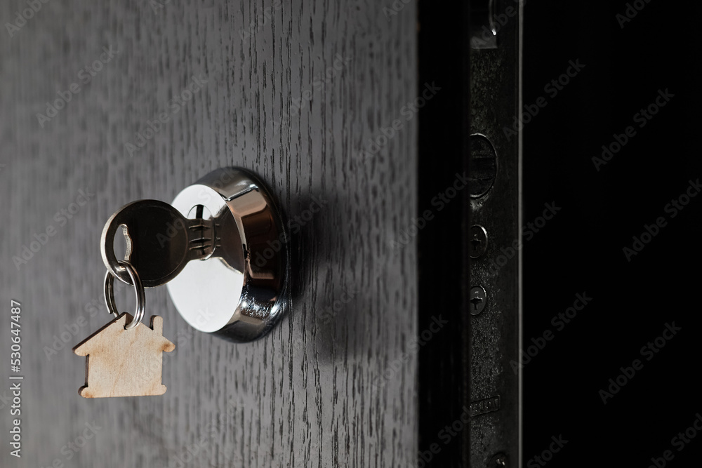 Key with a trinket in the form of a house in the door lock of an open ...