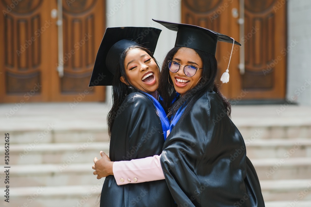 two young ladies in graduation costumes posing at camera at university ...