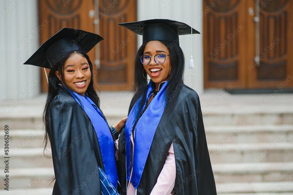 two young ladies in graduation costumes posing at camera at university ...