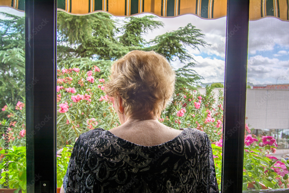Old Woman On The Balcony Of Her House. Rear view of a senior woman at ...
