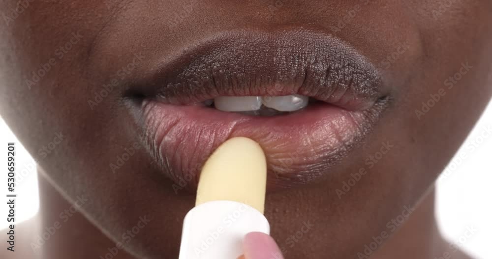 Close up view of an african woman applying lip balm to her lips and ...