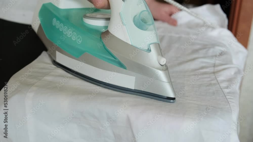 Female hand holding electric iron ironing clothes on ironing board ...