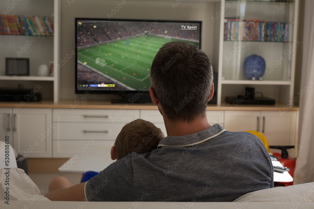 Caucasian father and son watching tv with football match on screen ...