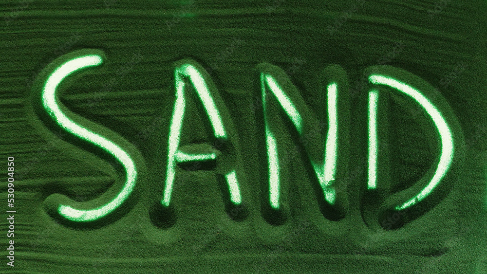 Hand drawing the Word Sand in the Green Sand. Male hand writes with ...