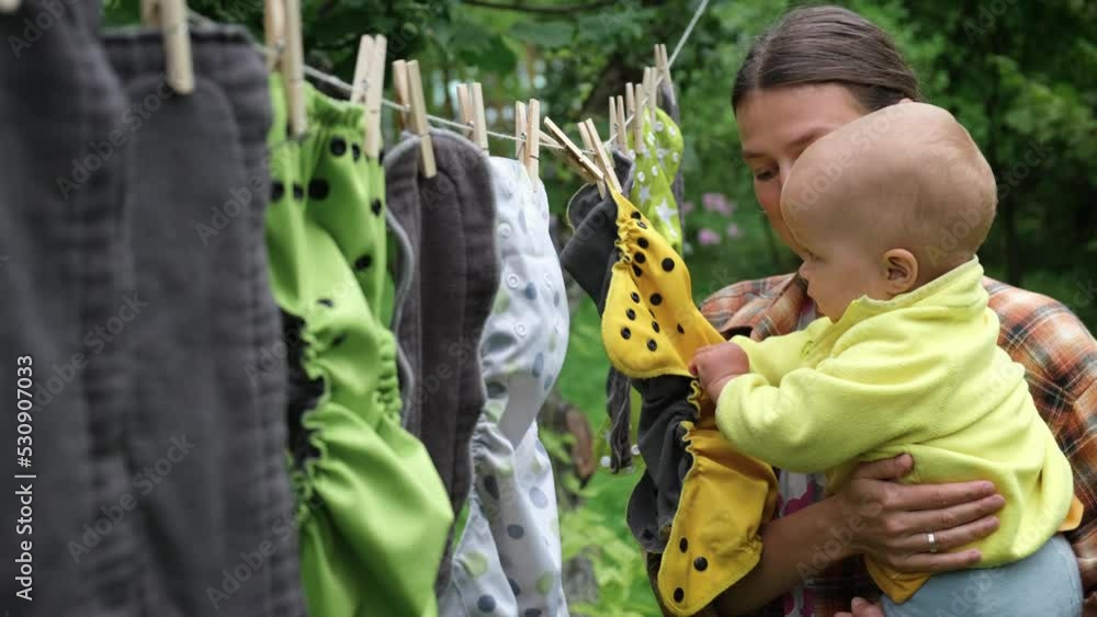 Mother with little baby removes reusable diapers drying on clothesline ...