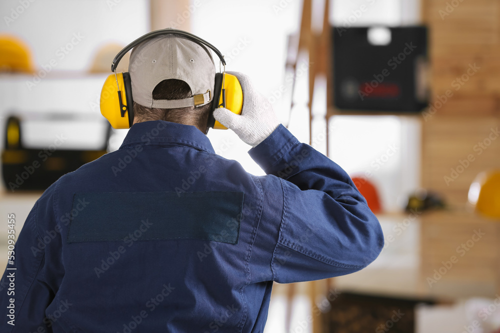 Worker wearing safety headphones indoors, back view. Hearing protection ...