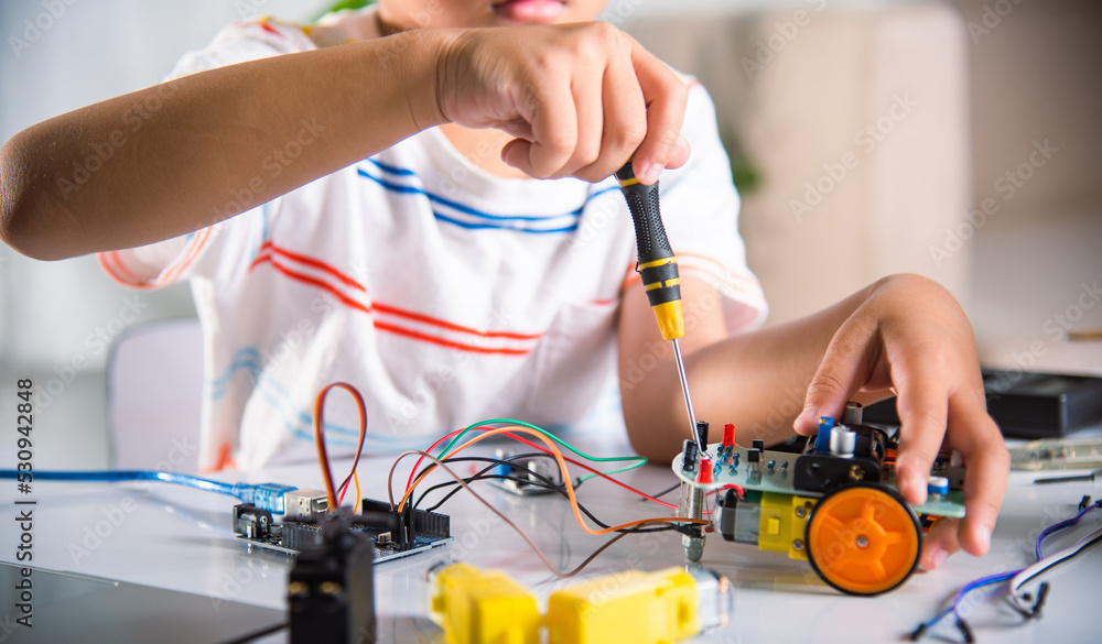 Asian kid boy assembling the Arduino robot car homework project at home ...
