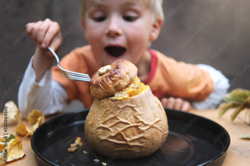 Happy excited little child boy with fork eating baked pumpkin stuffed ...
