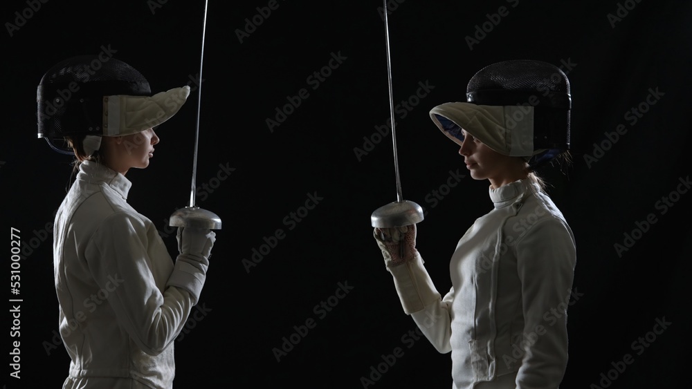 Side view of two young female swordswoman saluting with rapiers ...