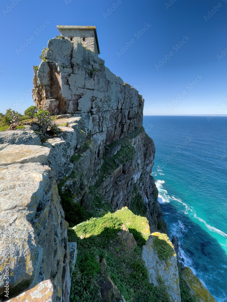 A breathtaking view of a small structure on top of a sheer stone cliff ...