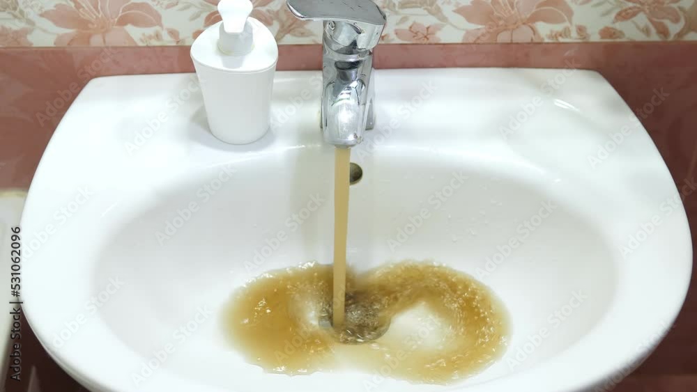 Woman's hand open the tap, rusty water running into a white sink ...