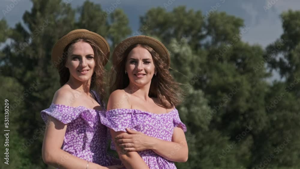 Portrait of two young twin girls in identical summer dresses and straw ...