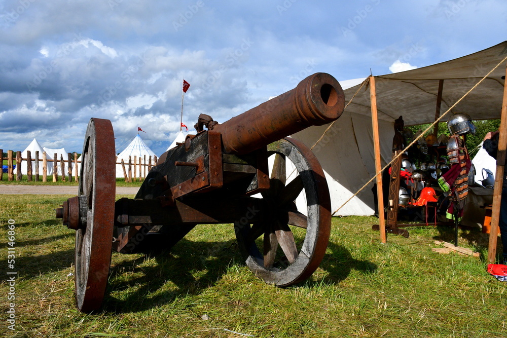 A close up on a rusty medieval cannon on wooden wheels seen next to a ...