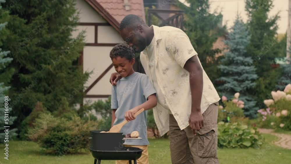 African dad and African son are cooking grilled vegetables near the ...