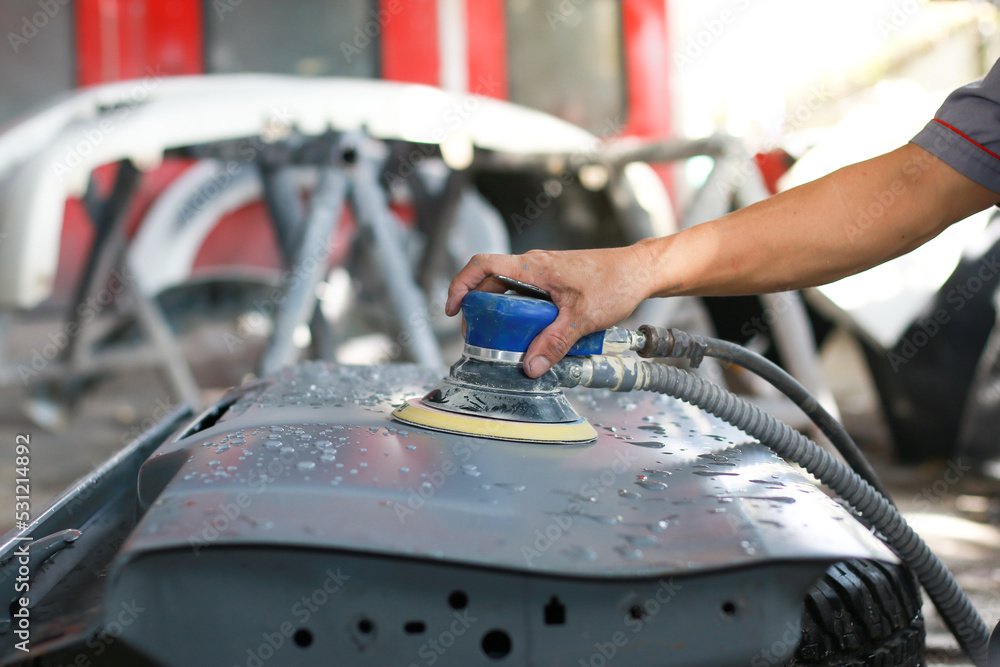 A mechanic with a sander is polishing the parts of the car to paint the ...