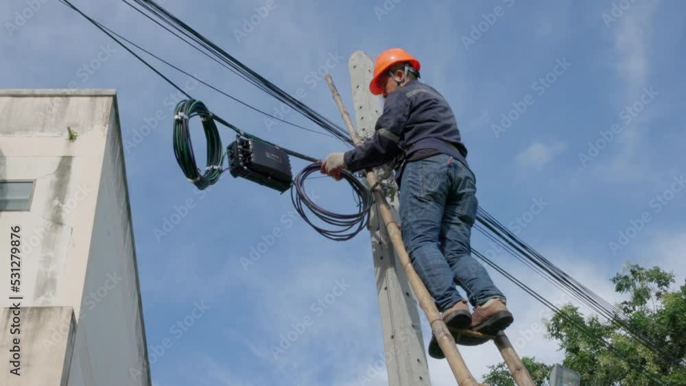 A telecoms worker is shown working from a utility pole ladder while ...