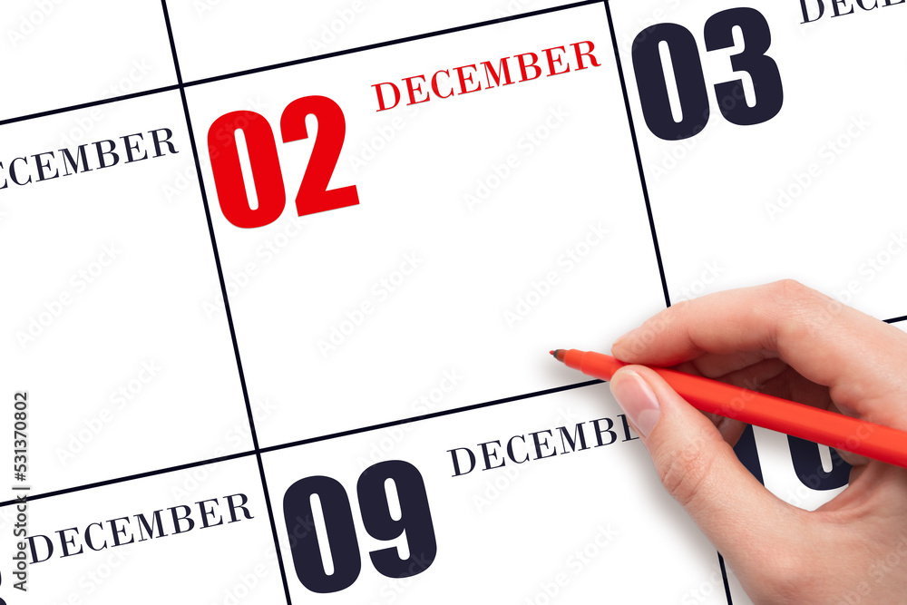 A hand holding a red pen and pointing on the calendar date December 2 ...