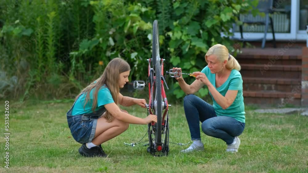 Mom helps her daughter fix her bicycle in the backyard of the house ...