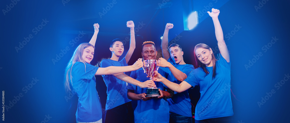 Multi cultural team winner of video games tournament. Holding big cup ...