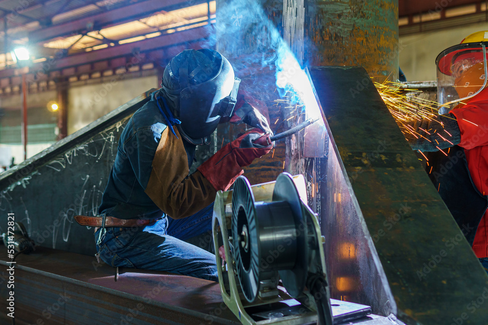 A welder is welding the stiffener of steel structuring with Flux-cored ...