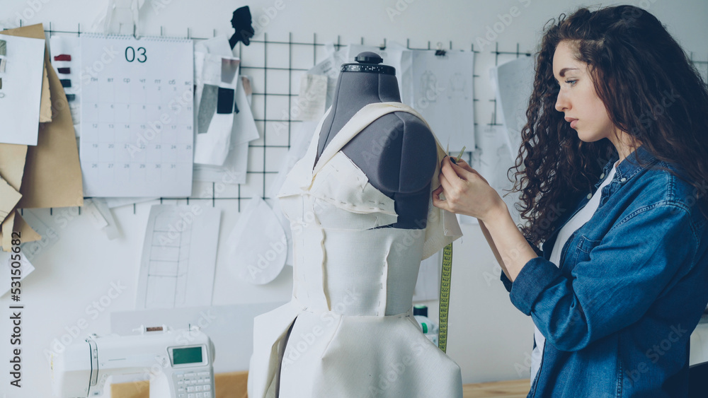 Young female tailor is adjusting clothes on tailoring dummy with sewing ...