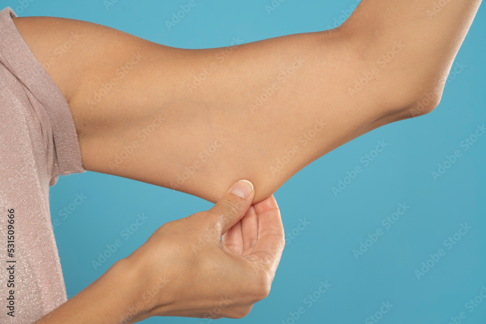 Close-up of a young tanned woman grabbing skin on her upper arm with ...