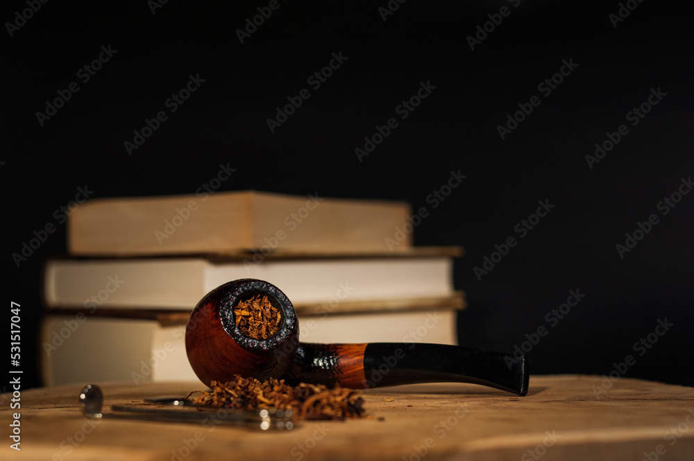 Tobacco pipe lying on a piece of wood with a pipe tamper and scattered ...