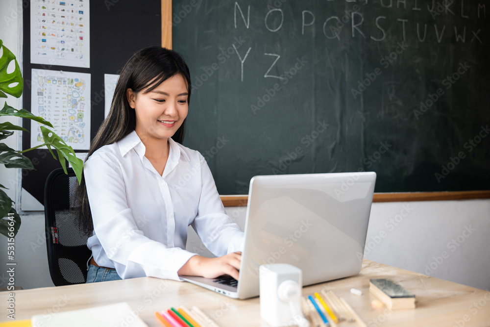 Back to school. Smiling female using computer sitting at school table ...