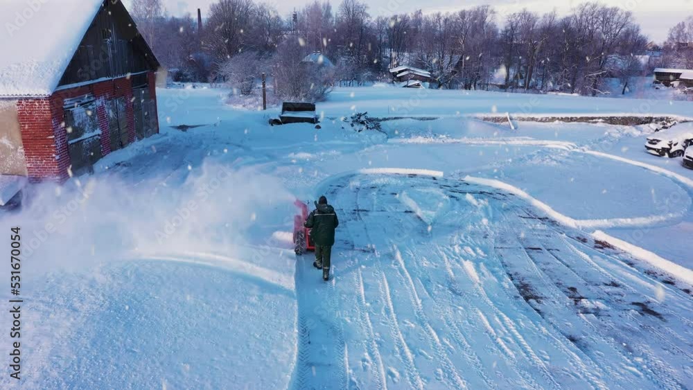 Man plowing snow with hand machine near old rural farm building, aerial ...