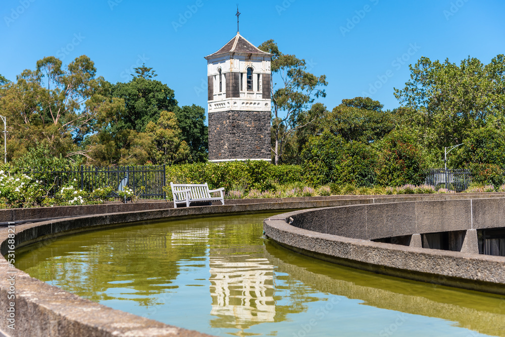 A square stone watchtower rises above the trees, while a circular pond ...