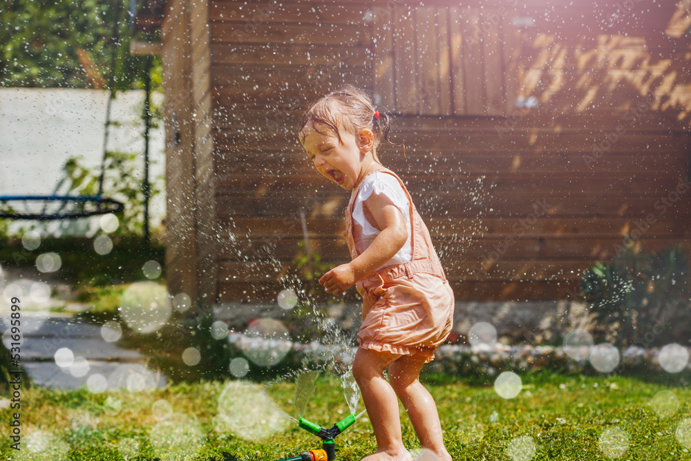 Beautiful girl in wet clothes play with sprinkler at garden Stock Photo | Adobe Stock