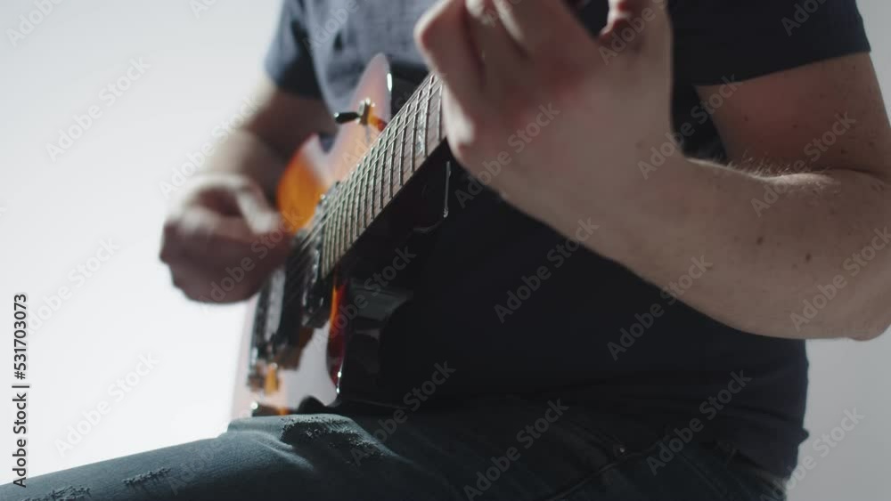 Man is sitting on chair in studio and playing an electric guitar, white ...