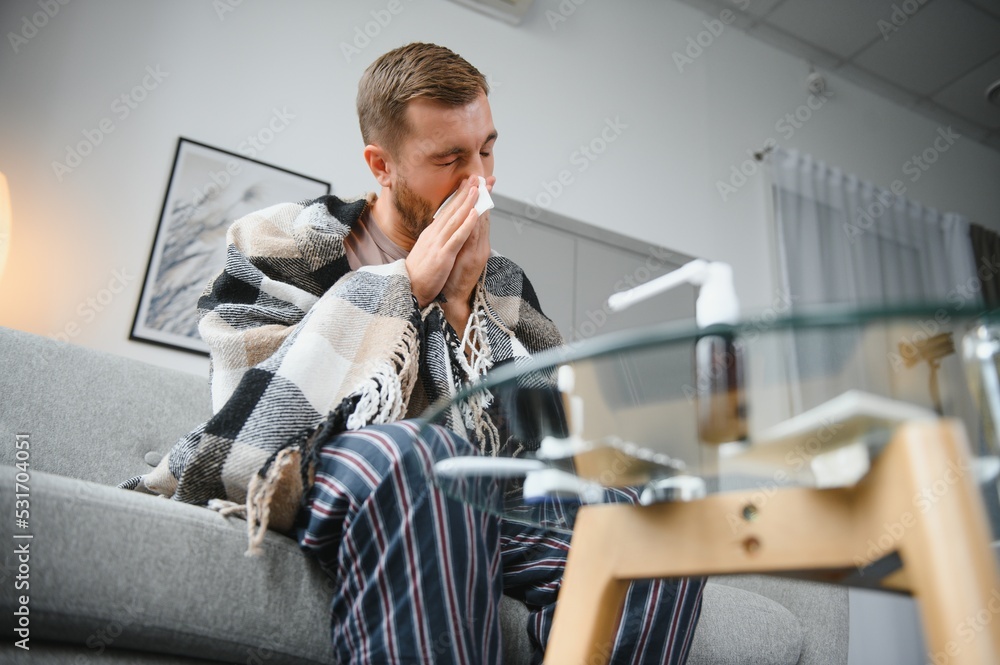 Young man suffering from a common cold and flu or allergy sit at home ...