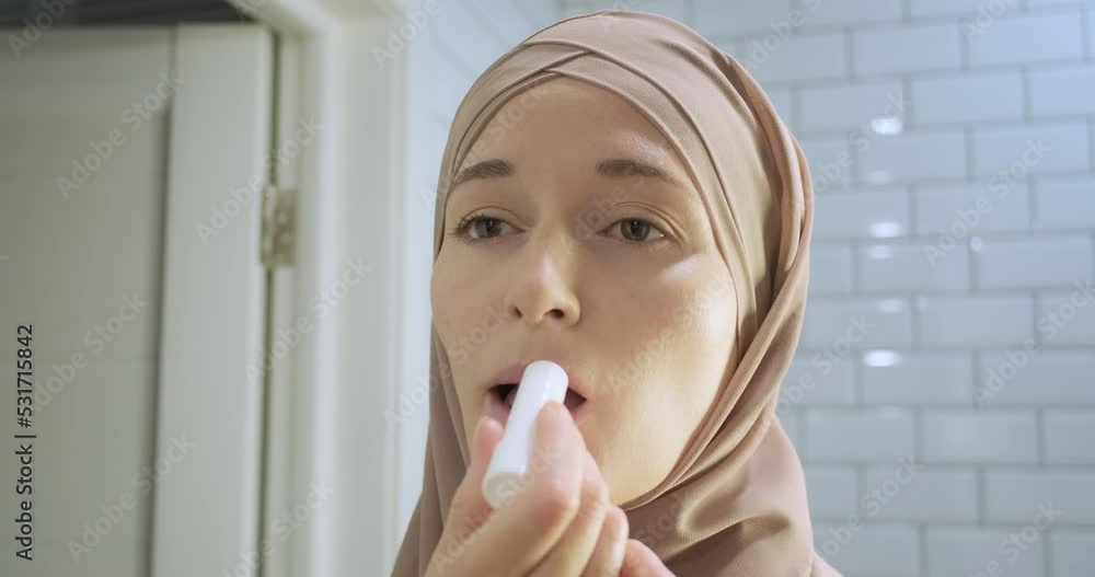 Female in hijab applies colorless lipstick to her lips. Close-up ...