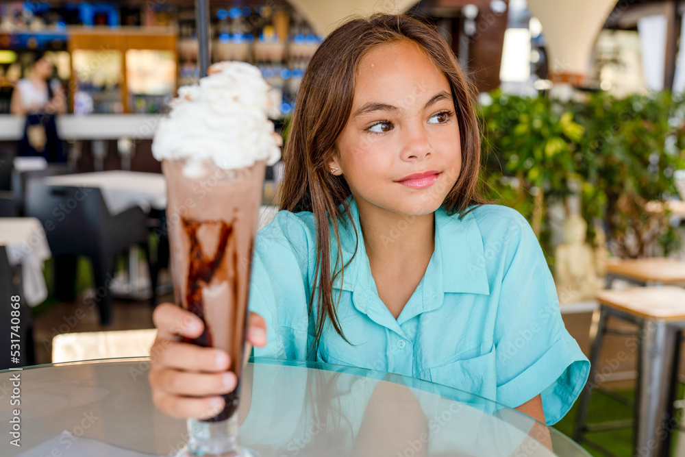 Beautiful child kid girl eating a chocolate shake in a restaurant. Cold ...