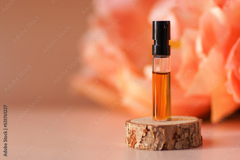 Perfume sample with orange liquid on woooden podium with peonies in ...