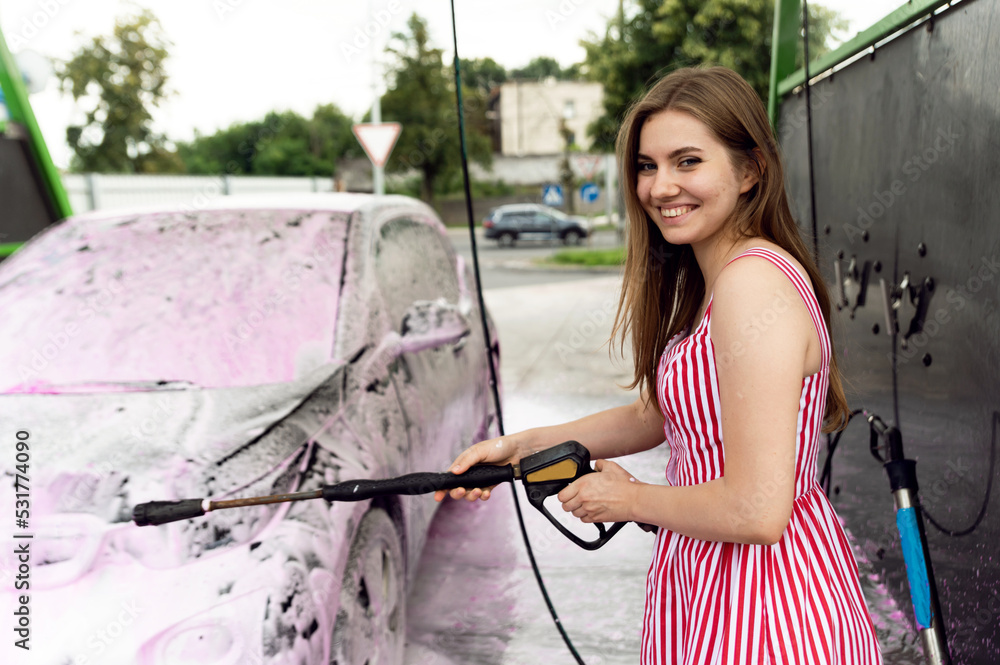 a beautiful girl washes an electric car at a car wash. pink foam on the ...