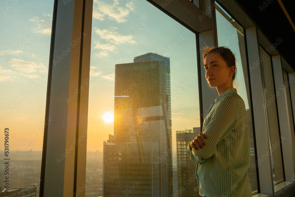 Portrait of smiling woman looking at cityscape through window of ...
