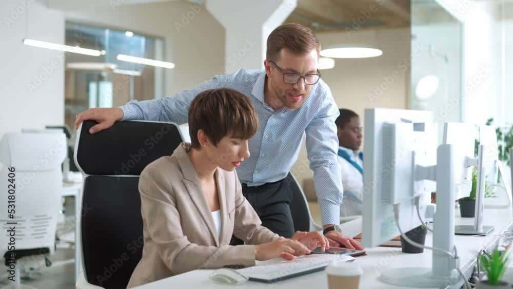 Office workers talking and typing on computer looking at screen indoors ...