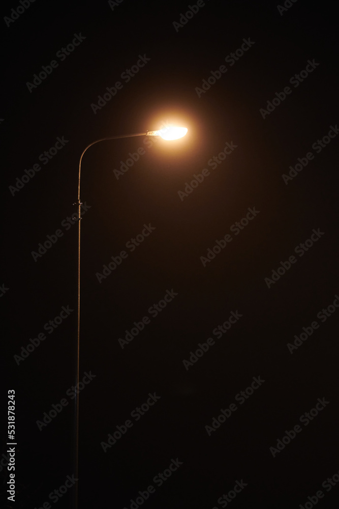 One night lamppost shines with faint mysterious yellow light through ...