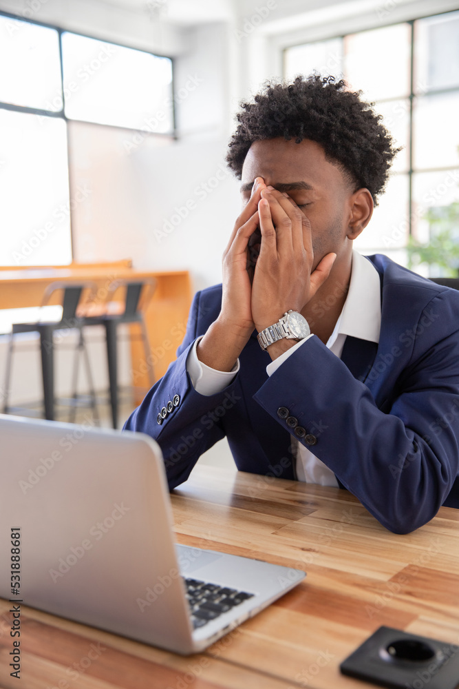Portrait of young tired office worker at table rubbing nose. Male model ...