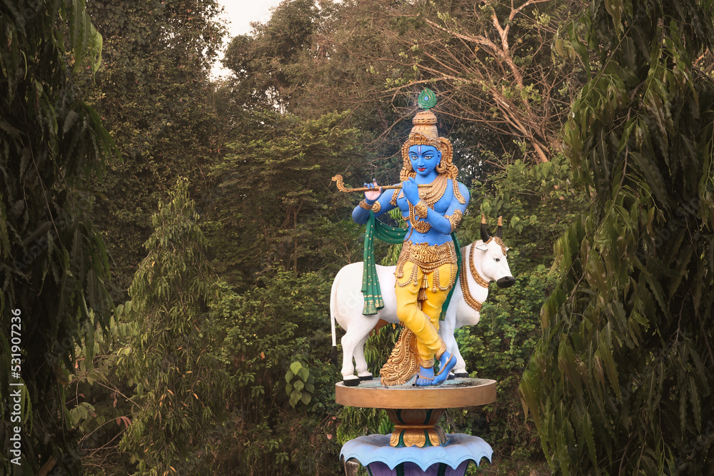 Statue of Krishna with a cow on a background of green jungle. Stock ...