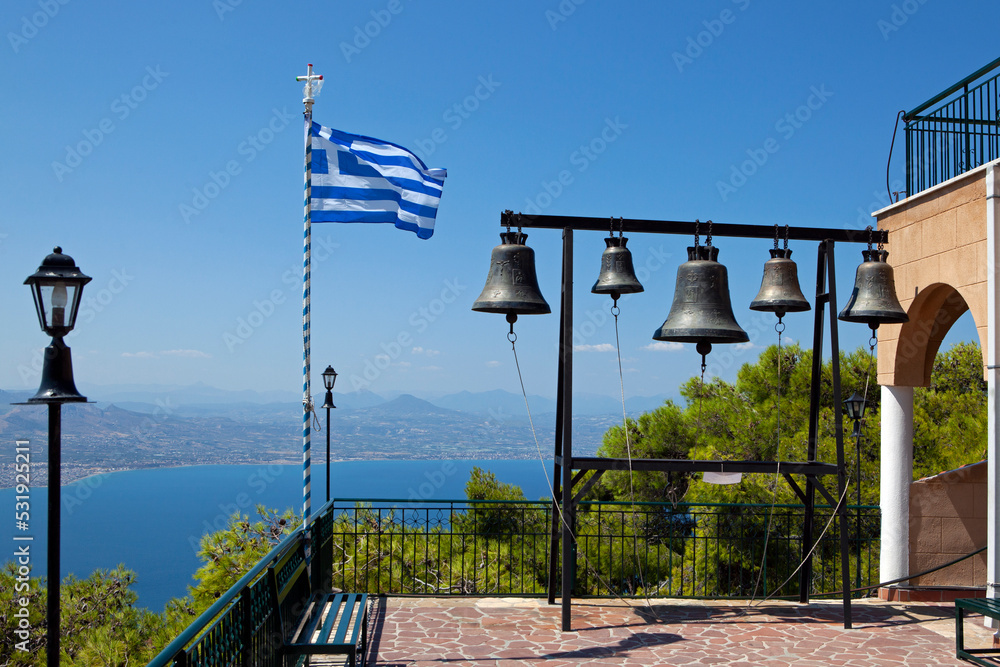 Greek flag on a pole with the Bells of Saint Patapios monastery in ...