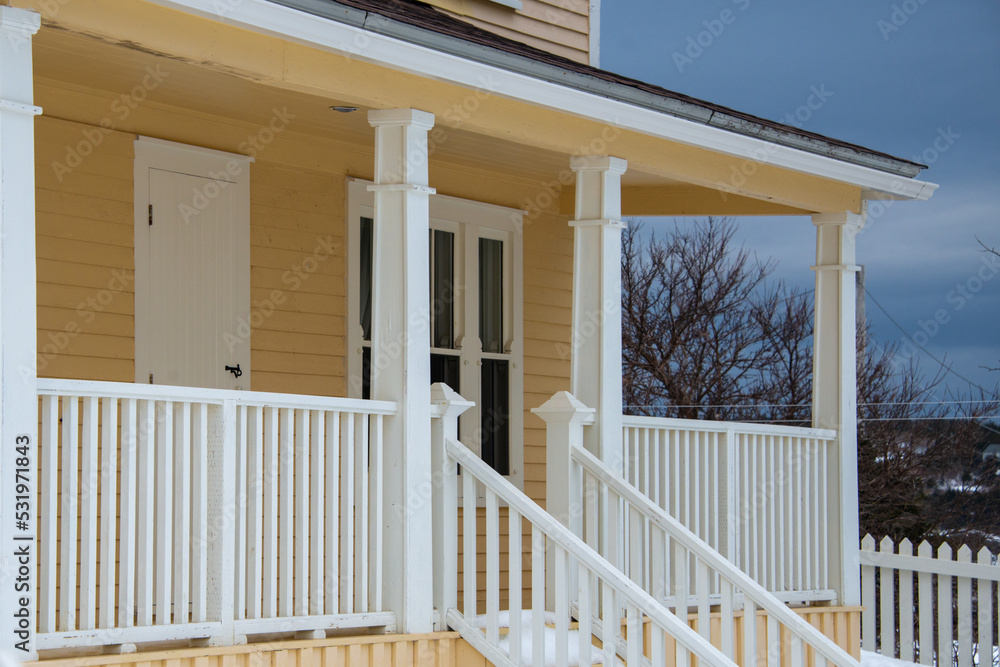 A yellow house with a front porch, white trim, windows, and a single ...