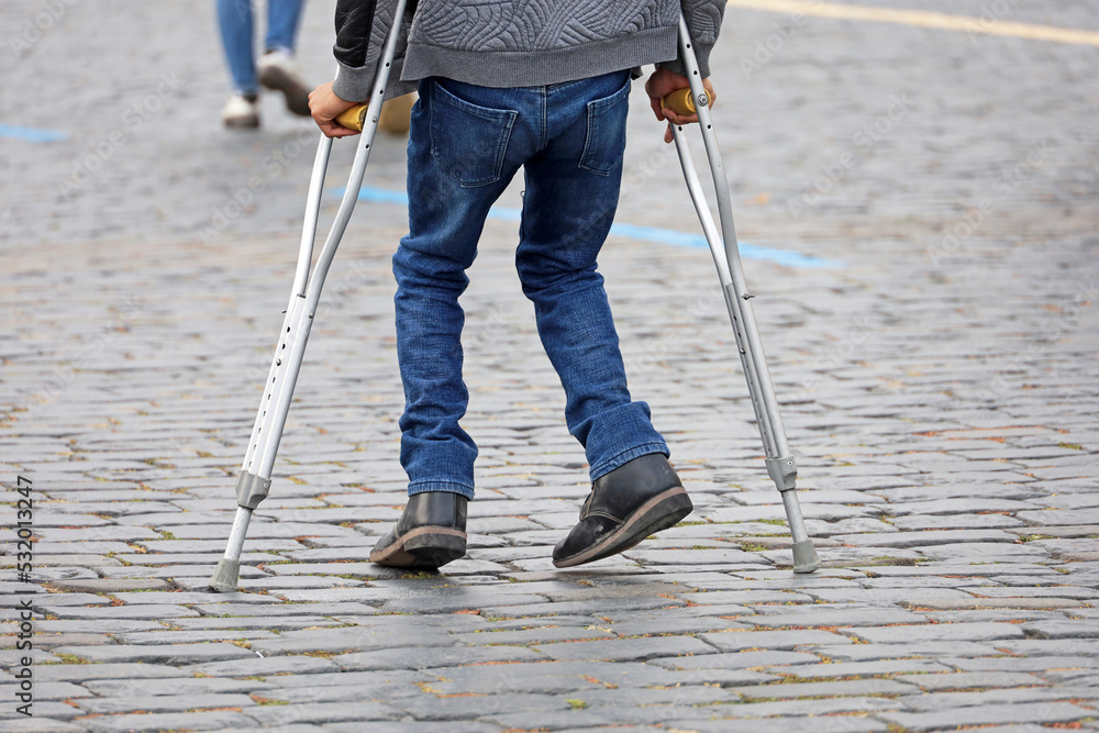 Man walking with crutches on a city street, male legs on sidewalk ...