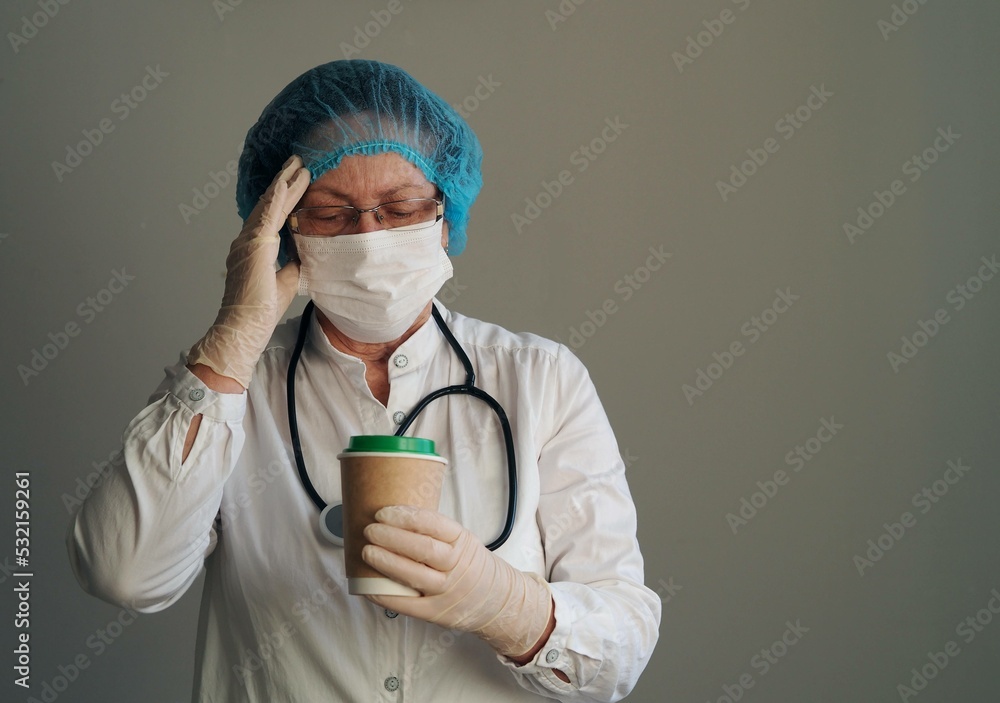 Tired female doctor after a difficult shift holding hot coffee in her ...