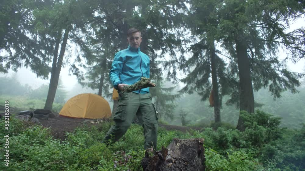 A man chops firewood with an ax in the forest while hiking in the ...