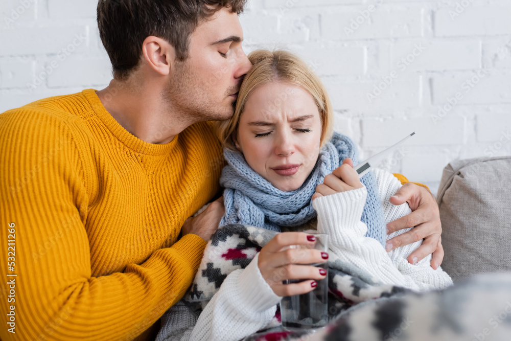 man hugging and kissing head of sick blonde woman with glass of water ...